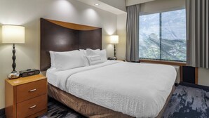 Quarto de hotel com uma cama grande, duas mesas de cabeceira com luminárias, uma cabeceira de madeira e uma janela ampla com cortinas.
