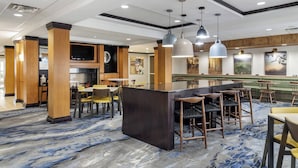 Um lobby moderno de hotel com área de bar, assentos e uma tela grande.