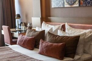 Quarto de hotel com cama, almofadas, escrivaninha e cadeira.