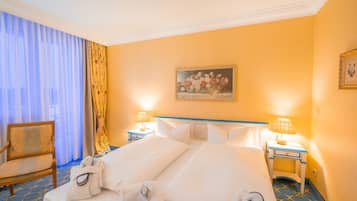 Quarto de hotel com uma cama grande, duas mesas de cabeceira com abajures, uma cadeira e um quadro na parede.
