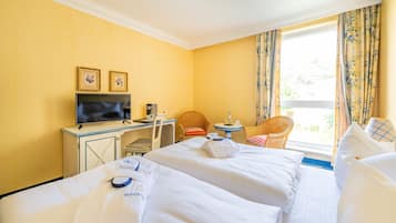 Quarto de hotel com duas camas, televisão, pequena mesa de escritório e janela com cortinas.