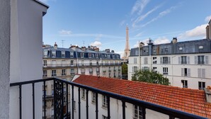 Vista da Torre Eiffel a partir de uma varanda, com um edifício em primeiro plano e telhado de telhas vermelhas.