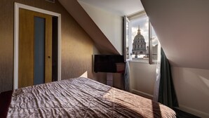 Quarto de hotel com cama, televisão, janela com vista para um edifício e porta.