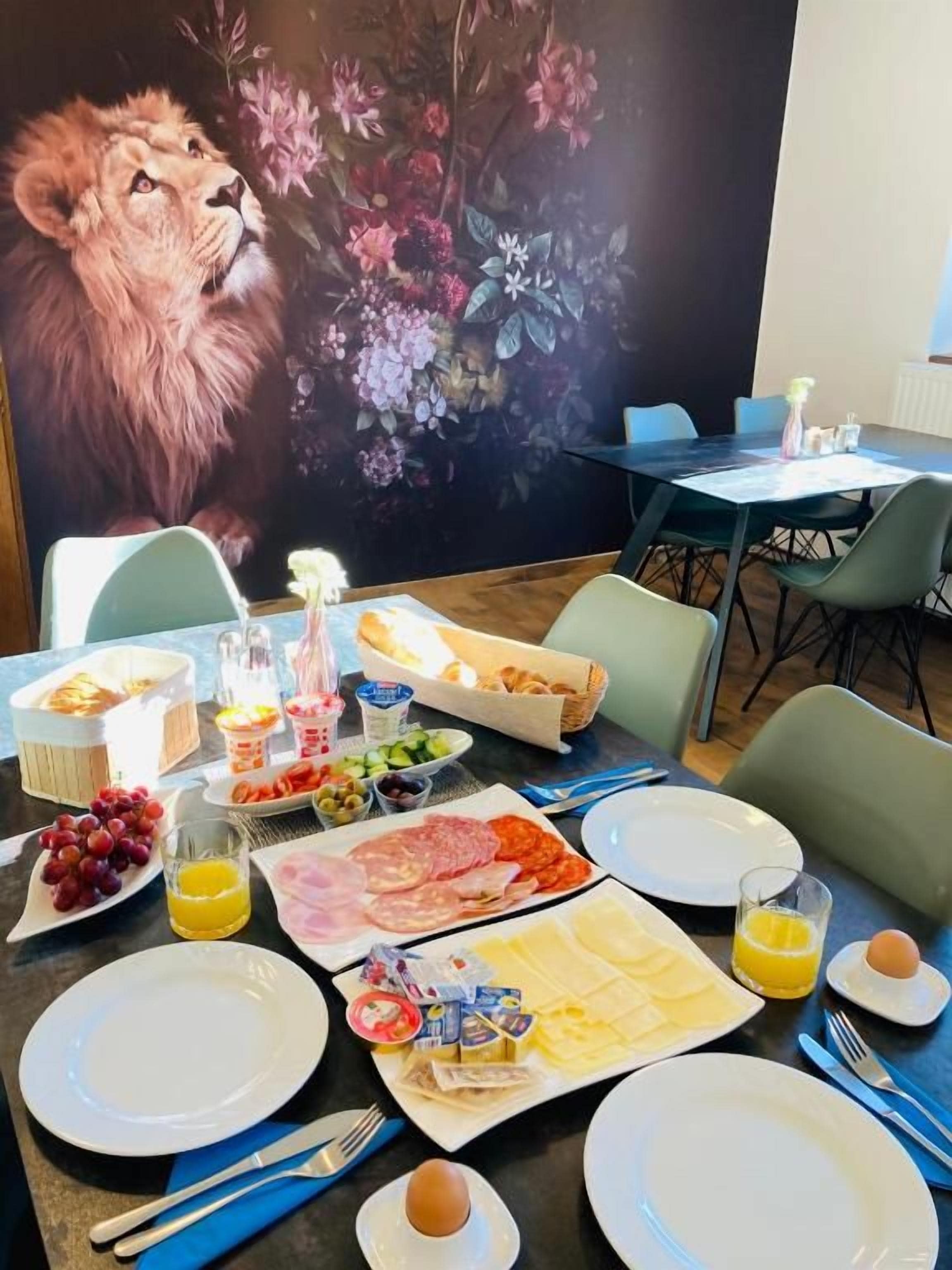 Mesa de café da manhã com mural de leão, cadeiras e diversos itens para o café.