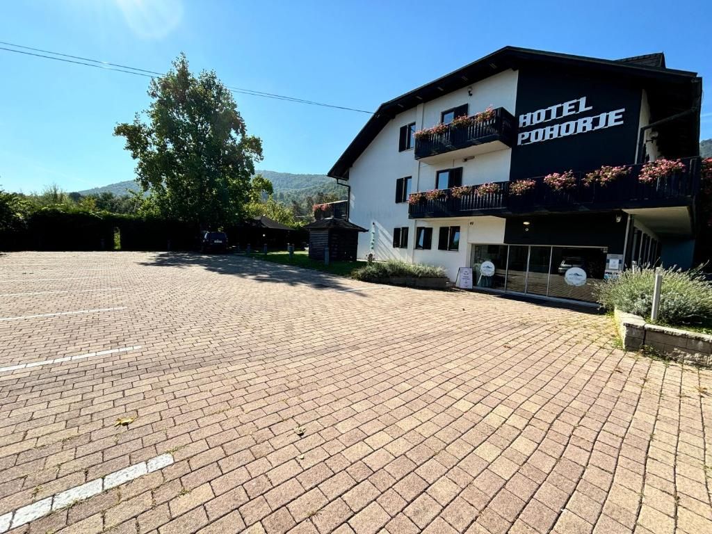 Hotel com placa de identificação, calçada e montanhas ao fundo.