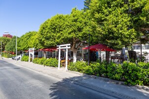 Rua com guarda-sóis vermelhos e pilares brancos, provavelmente marcando área de estar ao ar livre para um café ou restaurante.