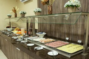 Buffet com diversos alimentos, incluindo carnes e frutas, e um expositor de vidro.