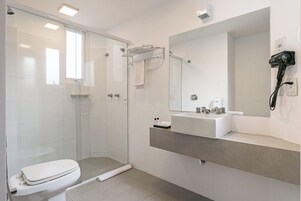 Casa de banho moderna com cabine de duche em vidro, sanita branca, espelho grande e secador de cabelo fixado na parede.