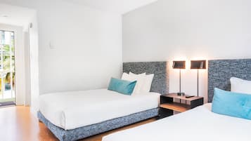 Quarto de hotel com duas camas, uma mesa de cabeceira e uma luminária na parede.