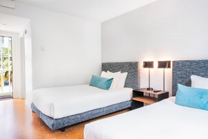 Quarto de hotel com duas camas, uma mesa de cabeceira e uma luminária na parede.