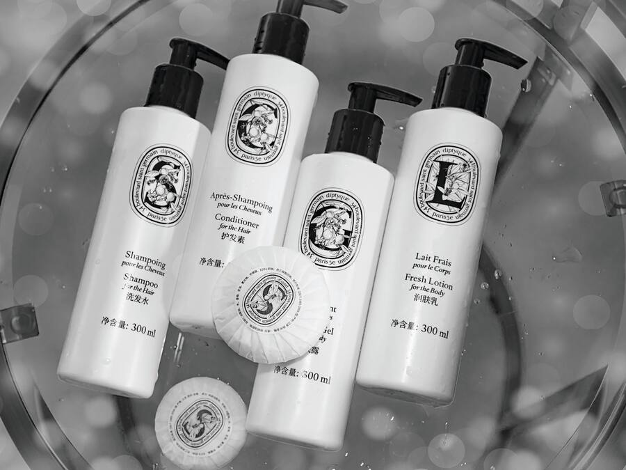 Quatro embalagens de produtos para cabelo e corpo em recipiente transparente.