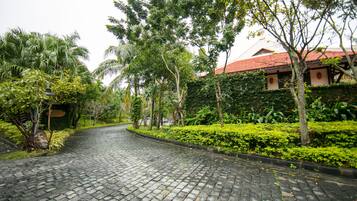 Uma rua de paralelepípedos ladeada por vegetação exuberante e um edifício com telhado de telhas vermelhas.