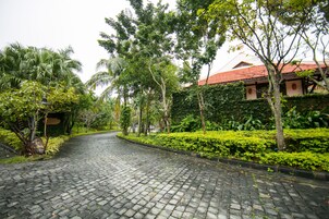 Uma rua de paralelepípedos ladeada por vegetação exuberante e um edifício com telhado de telhas vermelhas.