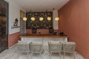 Uma área de bar moderna com balcão de madeira, três luminárias pendentes e cadeiras de vime.