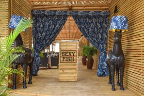 Interior em madeira com uma placa que diz 'SEXY FISH', duas estátuas de cavalos e cortinas estampadas.