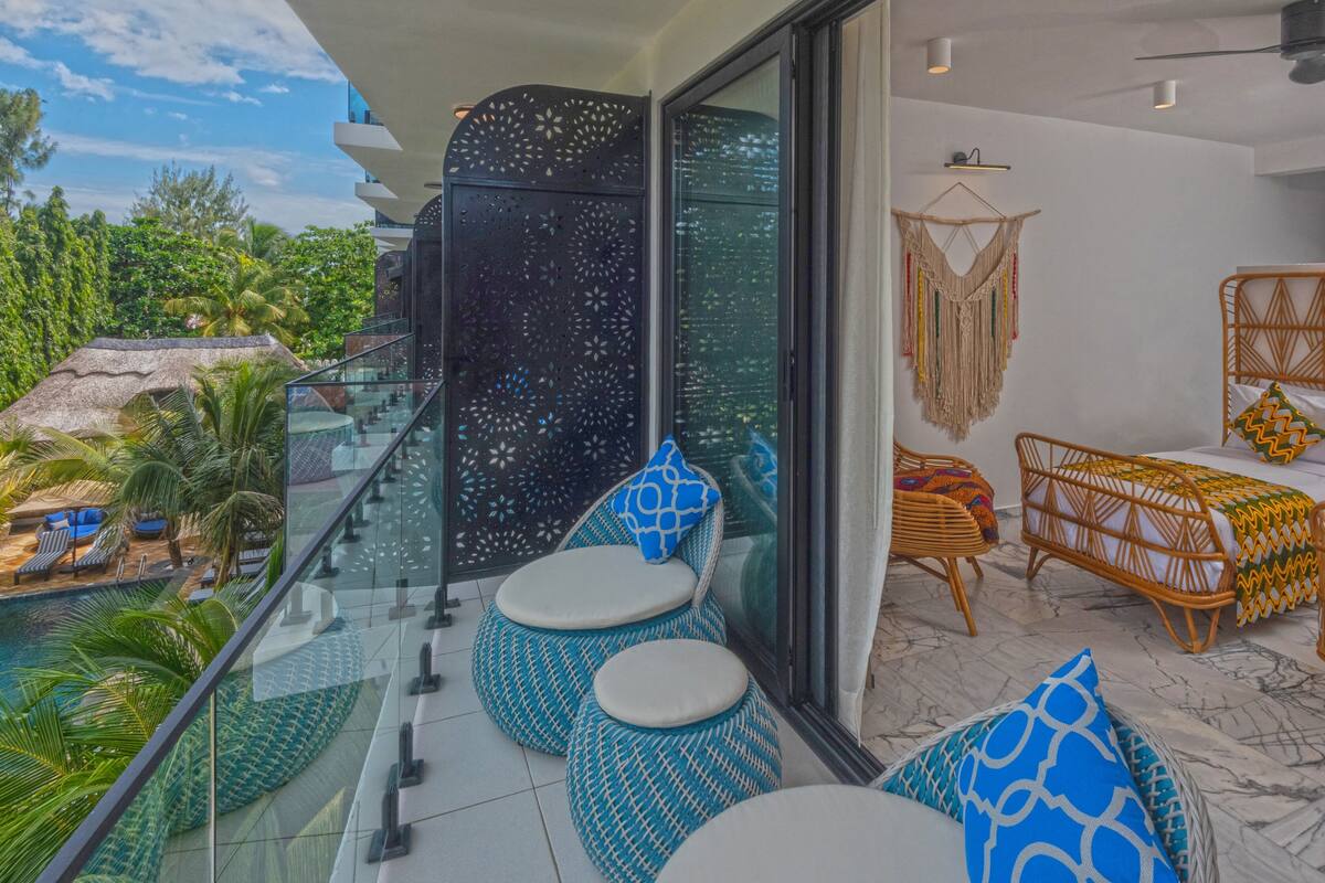 Varanda com grades de vidro, móveis de vime e vista para uma piscina e vegetação.