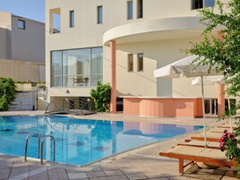 Piscina com espreguiçadeiras e guarda-sóis, cercada por um edifício com grandes janelas e fachada curva.