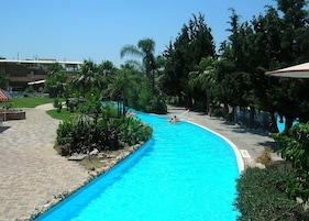 Piscina com borda curva, rodeada por vegetação exuberante e um caminho pavimentado.
