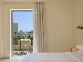 Quarto de hotel com varanda, uma cama, uma mesa e uma luminária.