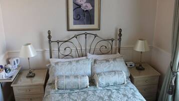 Uma cama bem arrumada com colcha estampada, duas mesas de cabeceira com luminárias, um quadro na parede e uma janela com cortinas.