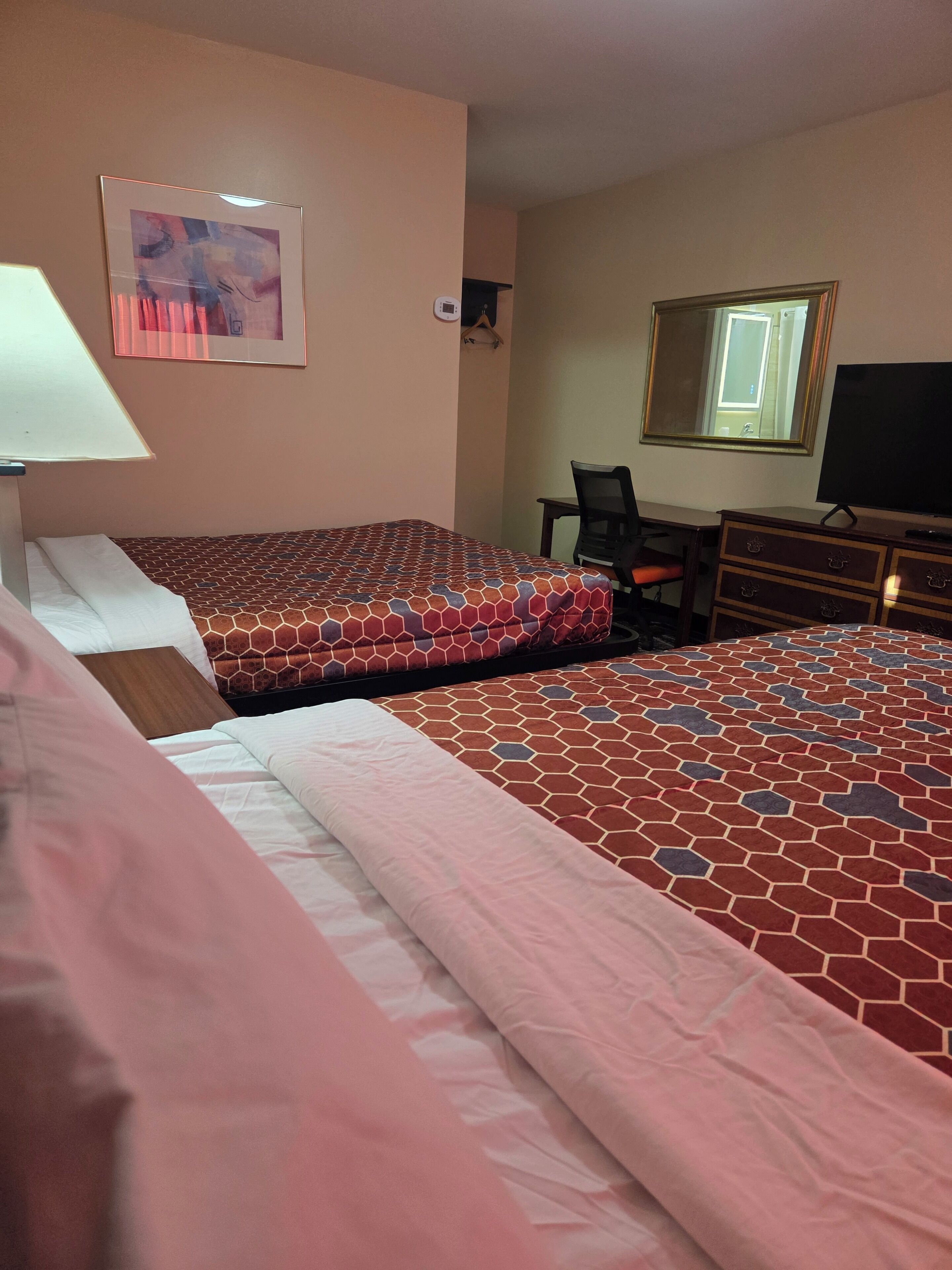 Quarto de hotel com duas camas, uma escrivaninha, uma cadeira, uma televisão e um espelho.