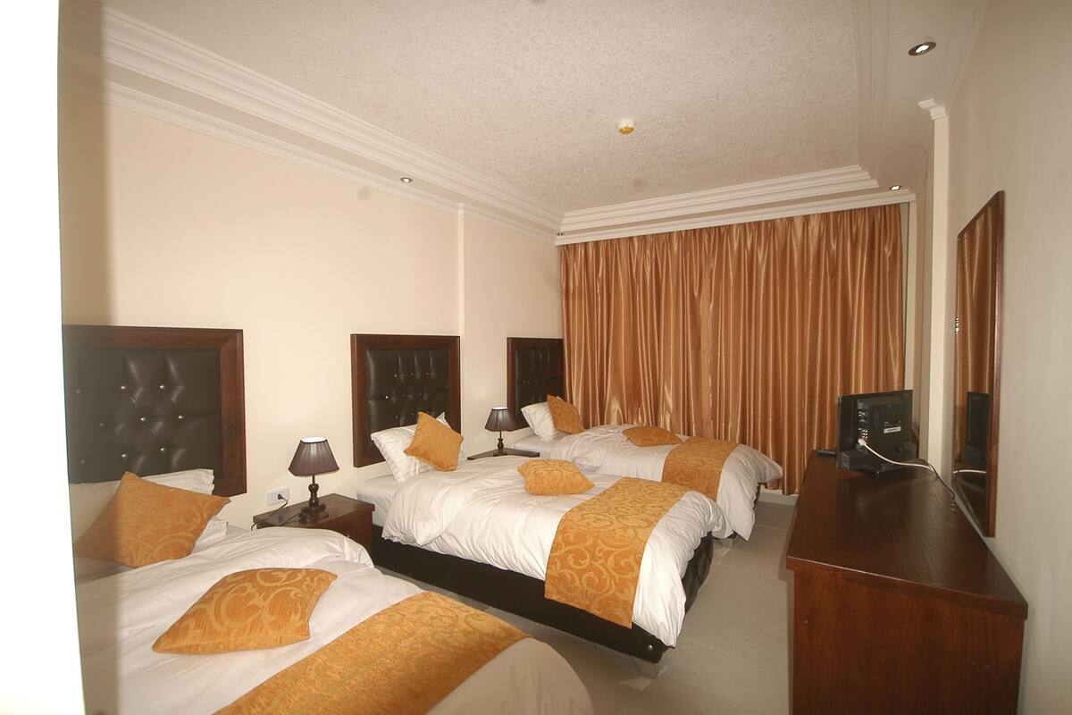 Quarto de hotel com três camas, uma escrivaninha e uma televisão.