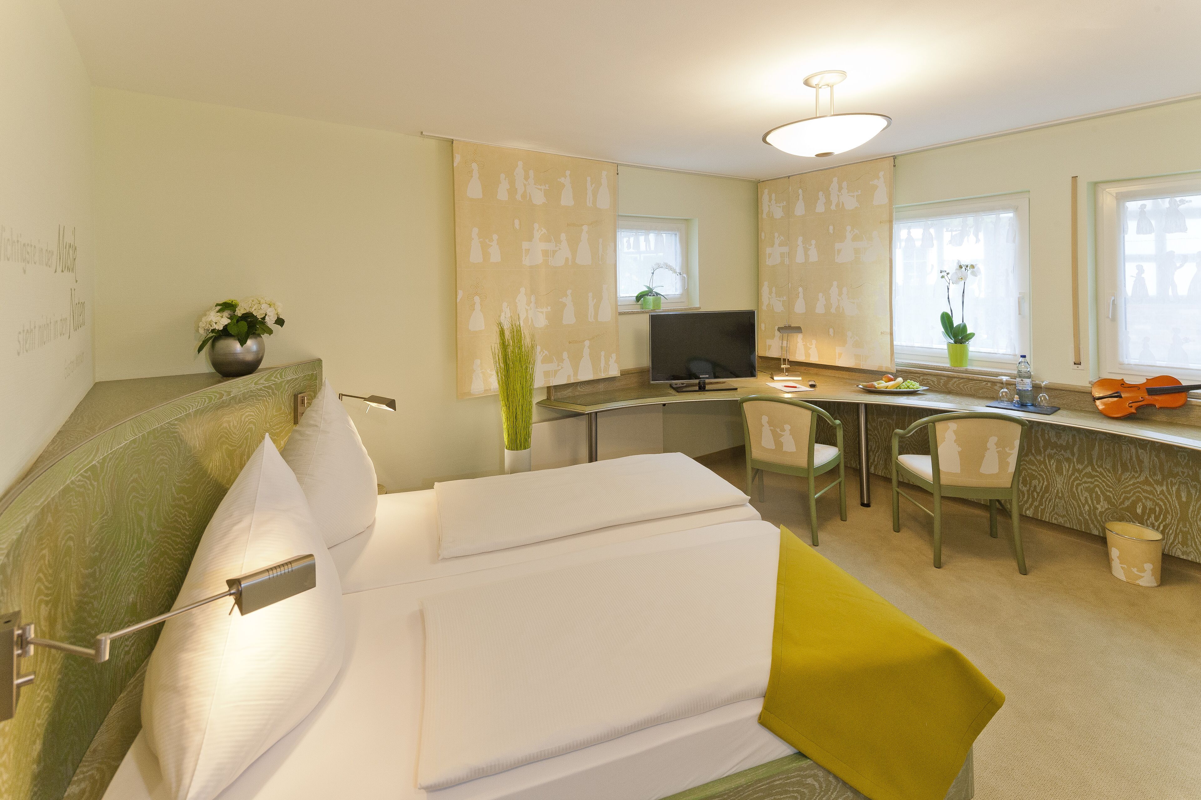 Quarto de hotel com cama, escrivaninha, cadeira, televisão e janela com cortinas.