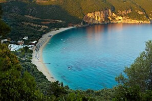Vista costeira com praia, barcos e um penhasco.