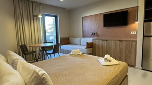 Quarto de hotel moderno com uma cama grande, uma mesa de jantar, um sofá e uma TV fixada na parede.