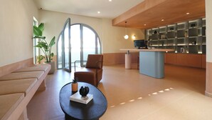 Uma sala de estar moderna com sofá, mesa de centro redonda, poltrona e área de cozinha com bancada e estantes.