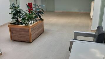 Quarto espaçoso com um cachepot de madeira com plantas, uma mesa branca e uma porta com o símbolo de número.
