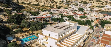 Hotel com piscina, situado em uma cidade costeira com montanhas ao fundo.