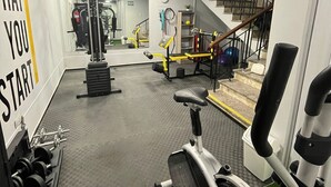 Uma academia com equipamentos de ginástica, um espelho e uma escada.