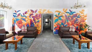 Ampla sala de estar com dois sofás, uma mesa de centro e um tapete. Um mural vibrante com padrão de folhas divide o espaço.