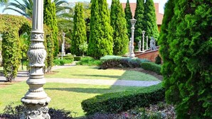 Um jardim bem cuidado com um caminho central, rodeado por sebes aparadas e árvores altas.