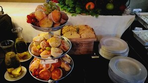 Uma mesa de buffet com diversos produtos de panificação, incluindo muffins e pastéis, e uma exposição de frutas.