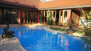 Uma piscina com deck ladrilhado, cercada por uma casa com telhado e janelas amplas.
