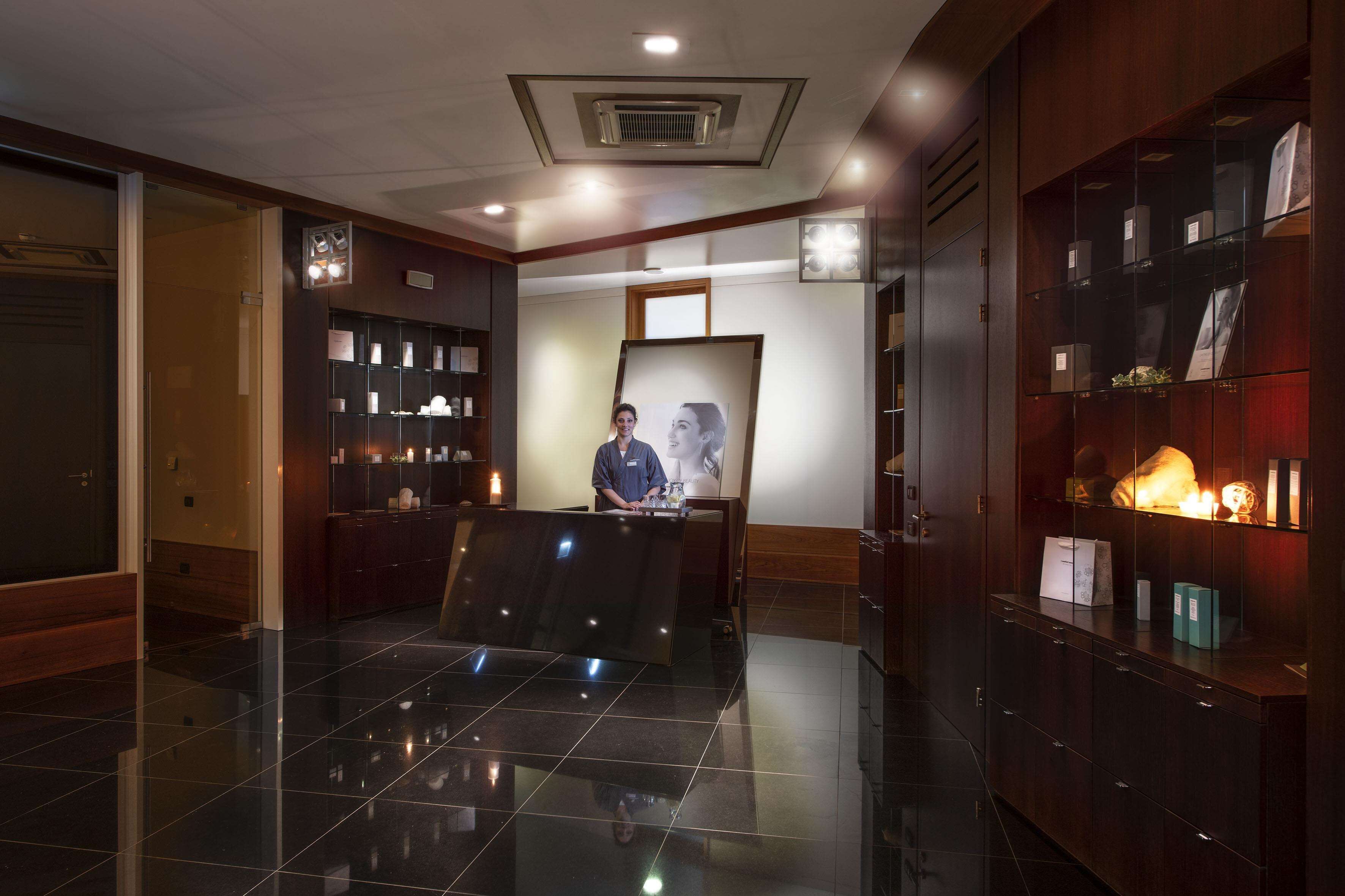 Uma área de recepção com piso preto polido, armários de madeira com vitrines de vidro e um quadro grande emoldurado na parede.