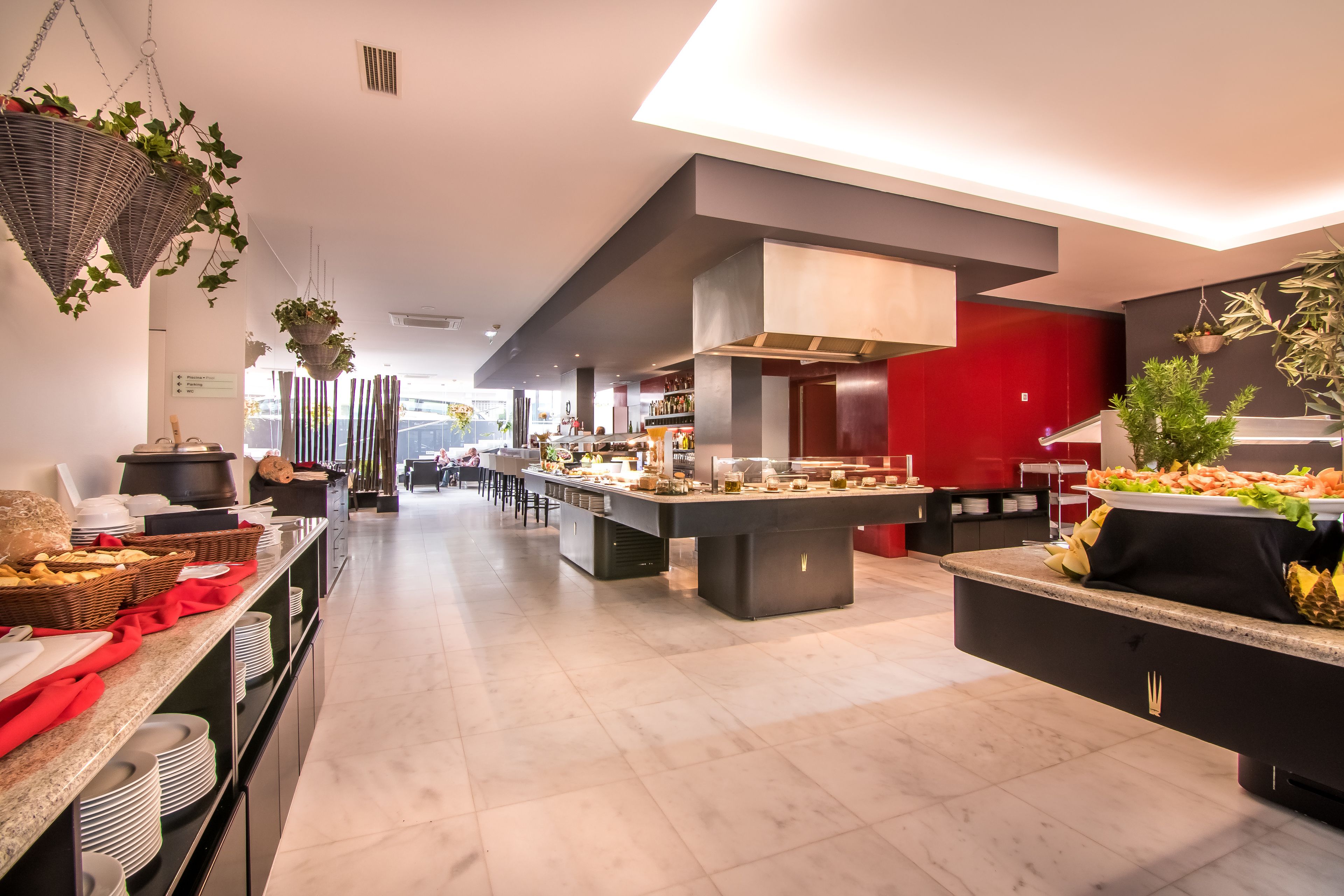 Cozinha moderna com bancada comprida, plantas penduradas e uma parede com detalhes em vermelho.