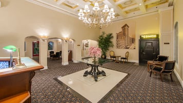 Um hall de hotel com um candelabro, um balcão de recepção, uma mesa com flores e uma placa com 'The Edmon'.