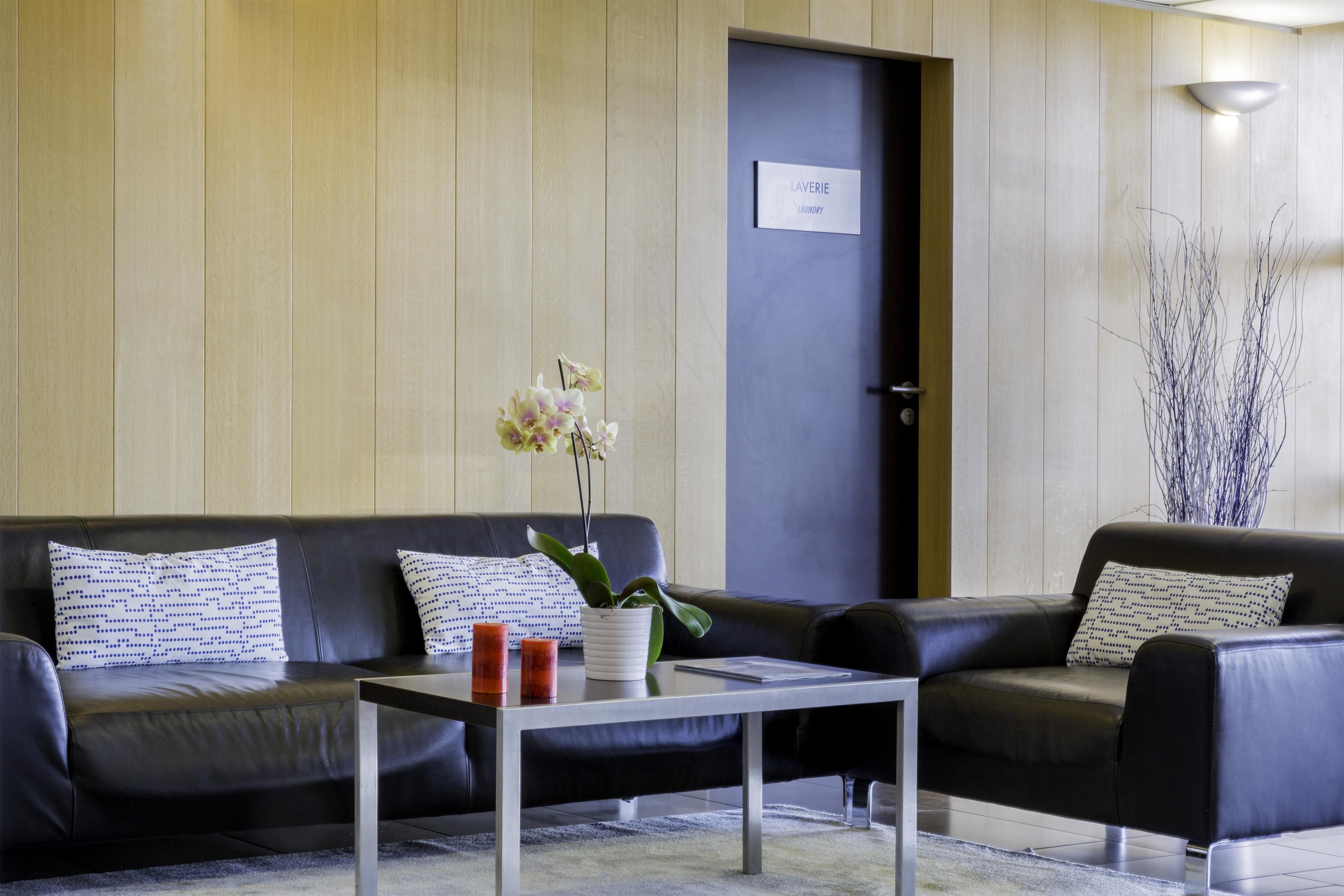Um lobby moderno de hotel com balcão de recepção, dois sofás, uma mesa de centro e uma porta com a inscrição 'LAVERIE'.