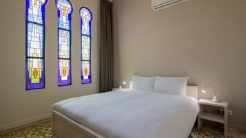 Quarto com uma cama grande, mesa de cabeceira, abajur e três janelas de vitrais.