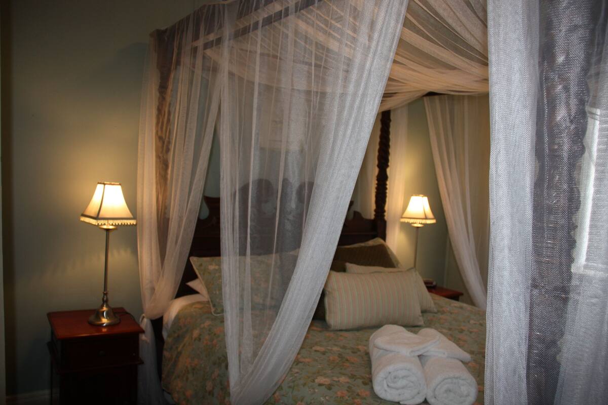 Quarto com cama de dossel, duas luminárias de cabeceira e toalhas dobradas na cama.
