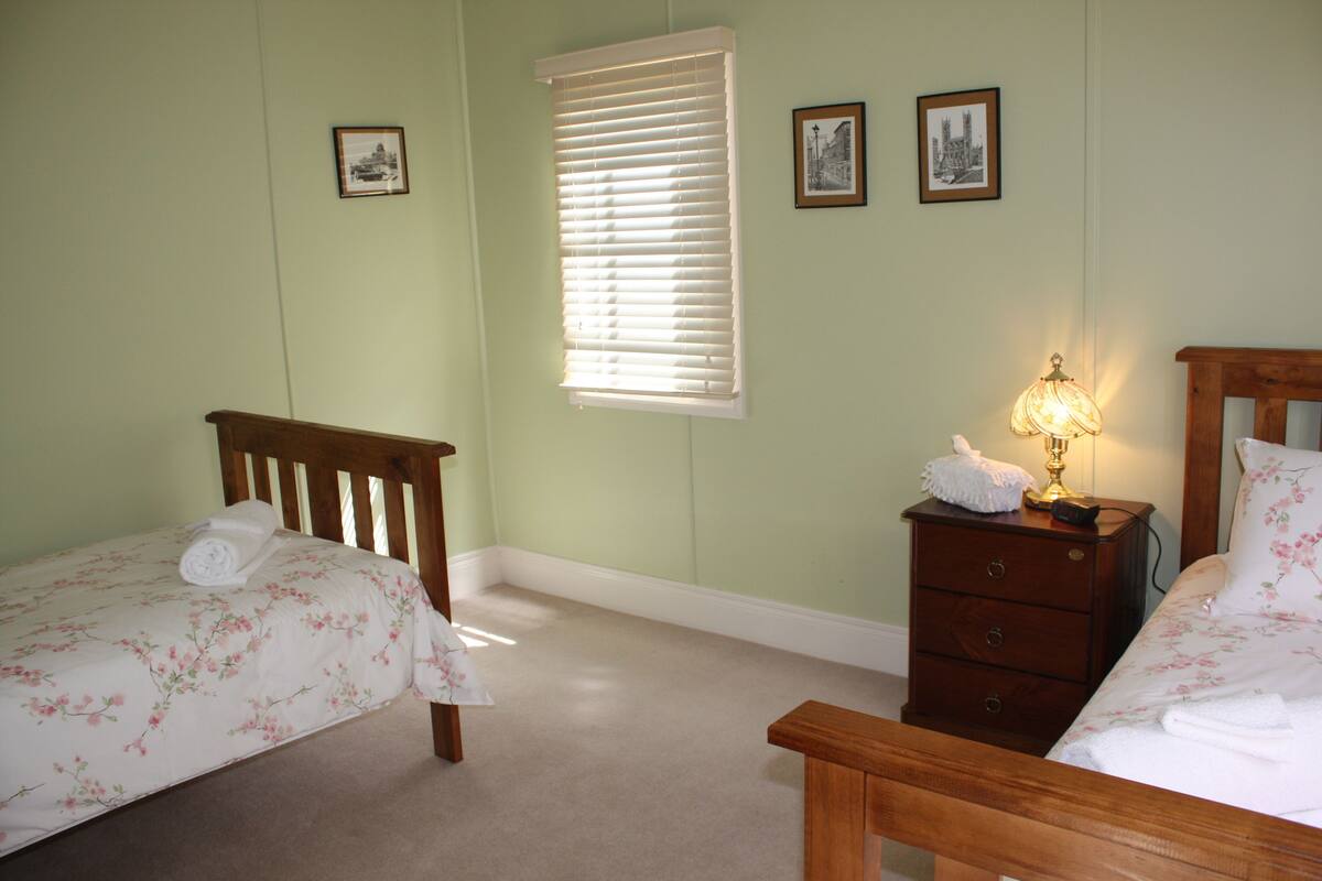 Quarto com duas camas de solteiro, mesa de cabeceira com abajur e cômoda.