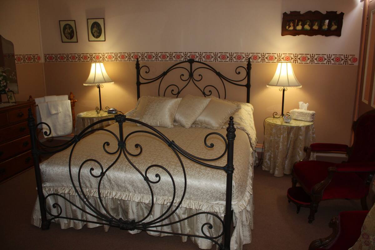 Quarto bem arrumado com cama, duas mesas de cabeceira, uma cadeira e um armário.