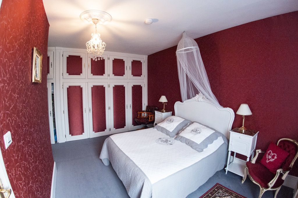 Quarto com cama, mesa de cabeceira, cadeira, guarda-roupa e um lustre.