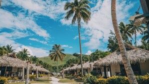 Um resort com palmeiras, casas de telhado de palha e um céu azul límpido.