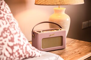 Um rádio antigo sobre uma mesa de cabeceira de madeira ao lado de um abajur.
