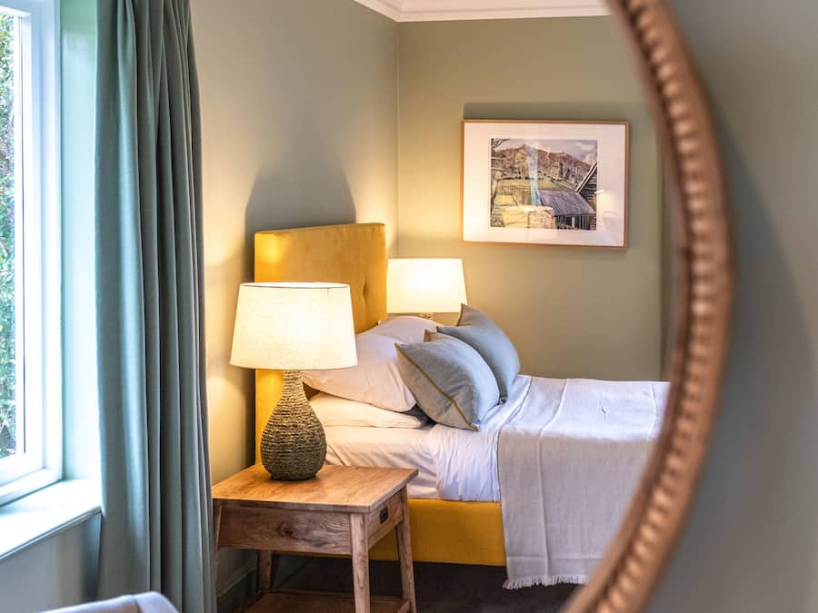 Quarto com cama, mesa de cabeceira, abajur e um quadro na parede.