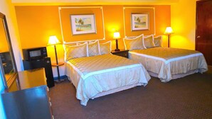 Quarto de hotel com duas camas, uma escrivaninha com computador e duas luminárias.